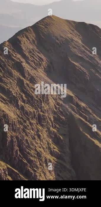 Sunlight illuminates the rugged mountain peaks. The landscape features ...