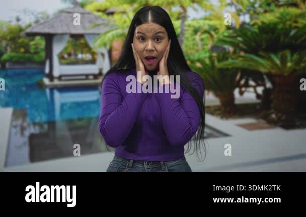 Woman holds cheeks with hands at hotel pool beside resort building ...