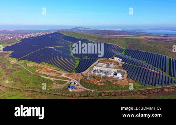 An expansive solar farm covers rolling hills, capturing sunlight with ...