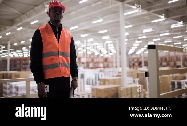 Confident warehouse worker wearing safety gear and holding documents ...