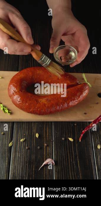 Person using a brush to apply oil to a large sausage placed on a wooden ...