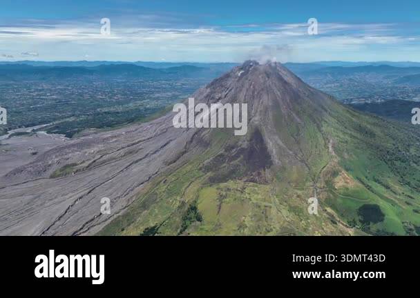 The volcano rugged slopes tower above rolling hills, black lava scars ...
