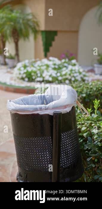 Metal trash can in sunny outdoor garden with blossoming flowers and ...