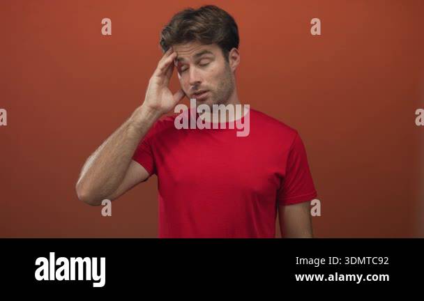 Man with hand pressed to forehead and closed eyes in orange studio ...