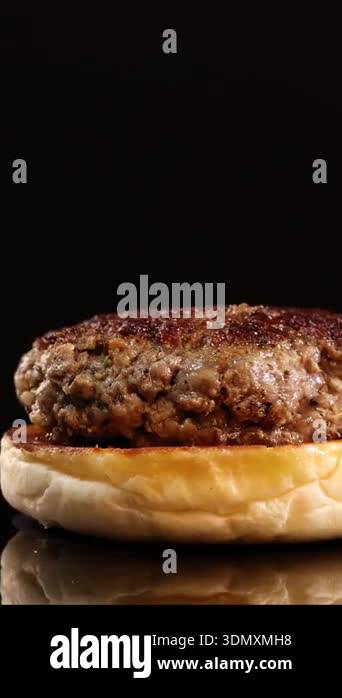 A single beef burger patty sits atop a toasted bun, rotating smoothly ...