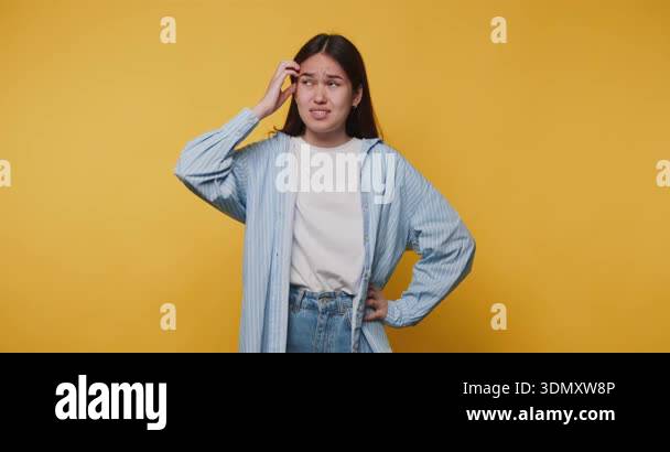 A young woman stands in front of a yellow background. She looks ...