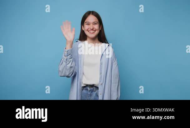 A young person is seen waving and smiling against a solid blue ...