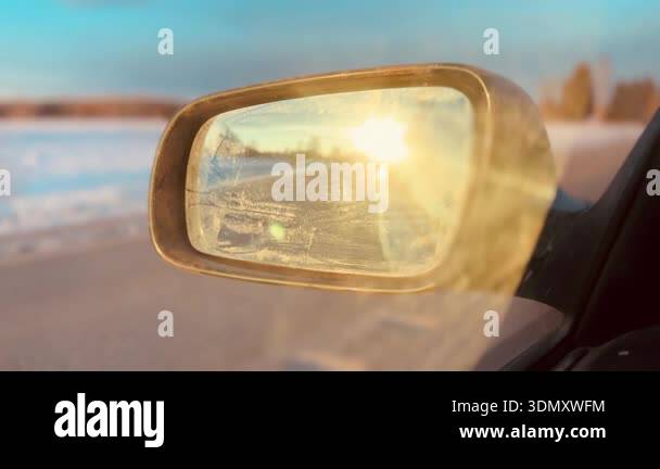 Close-up view of a car rearview mirror reflecting bright sun at sunset ...