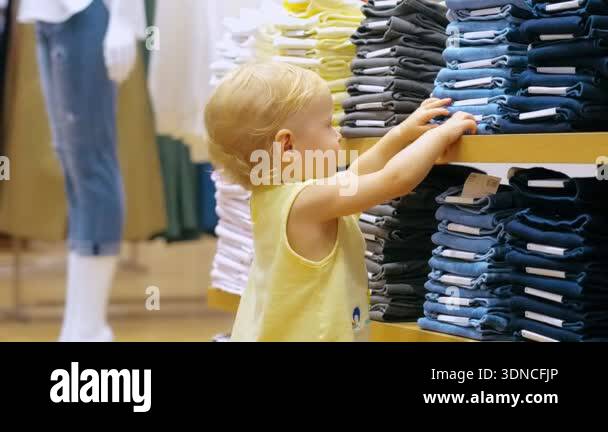 Little girl touching jeans lying on shelves in clothing store Stock ...