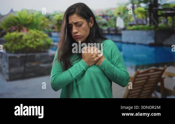 Young hispanic woman clutching chest with hands, grimacing at outdoor ...
