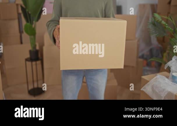 Man smiling while holding large cardboard box in bright empty building ...