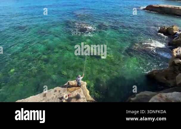 Sliema, Malta - February 8, 2026: A lone fisherman stands on a rocky ...
