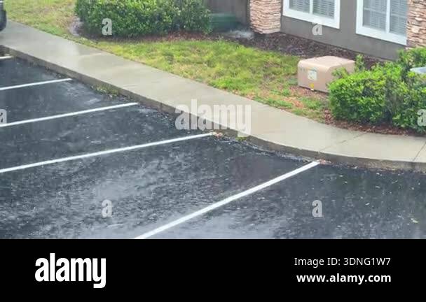 Heavy rain pours onto an empty parking lot and wet sidewalk beside a ...