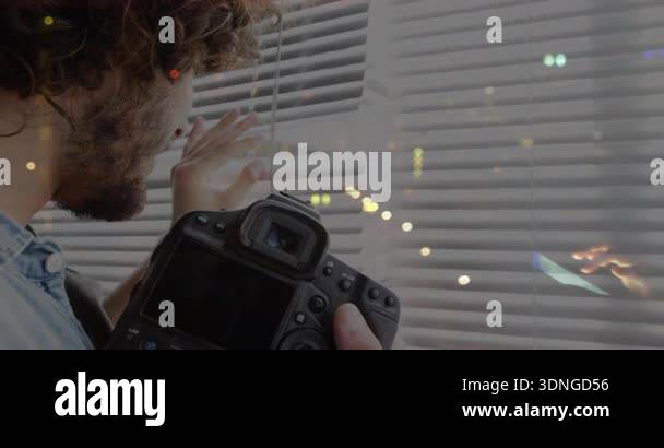 Photographer tilting blinds at window, revealing city lights and ...