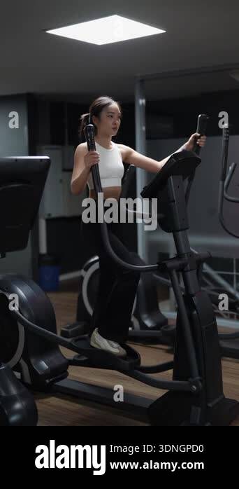 A determined and strong Asian woman is lifting weights at a fitness ...