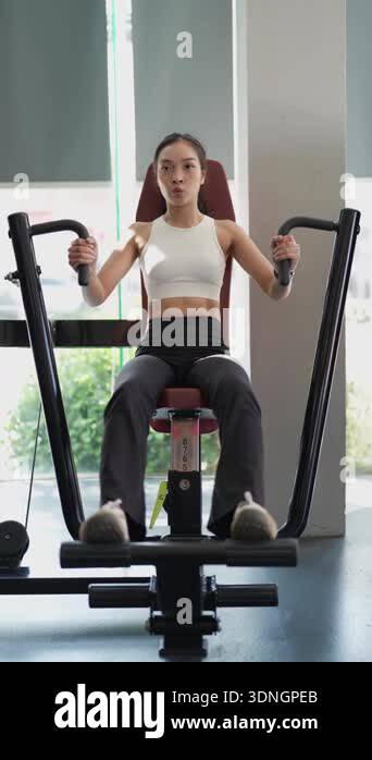 A determined and strong Asian woman is lifting weights at a fitness ...