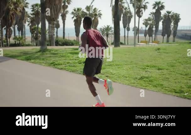 African American man running in a city park near the beach, training ...