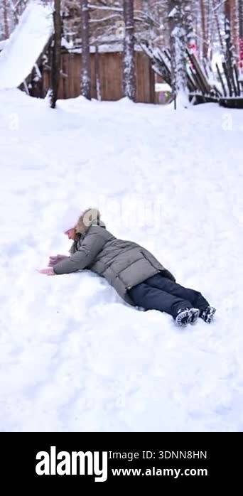 A young girl delights in playing in a snowy landscape, falling and ...
