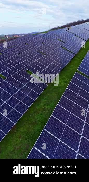 A field filled with solar panels spreads across a hillside under a ...