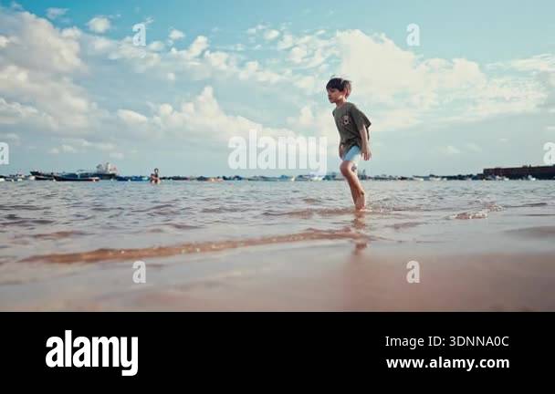 6 years old child walking along ocean shoreline on yellow sandy beach ...