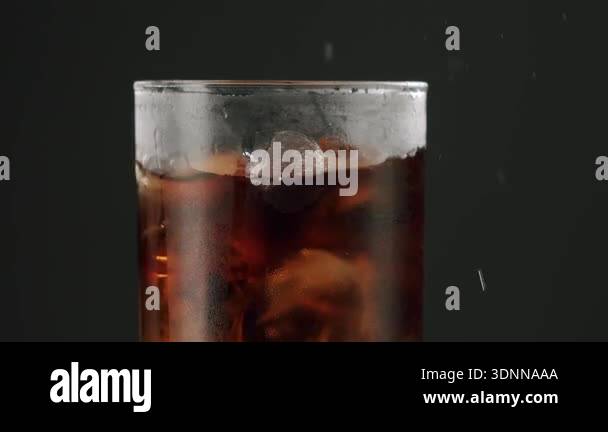 Single ice cube splashing into a cold, fizzy glass of dark soda ...