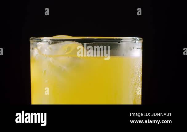 Close up slow motion shot of ice cubes falling into a cold glass of yellow carbonated orange ...