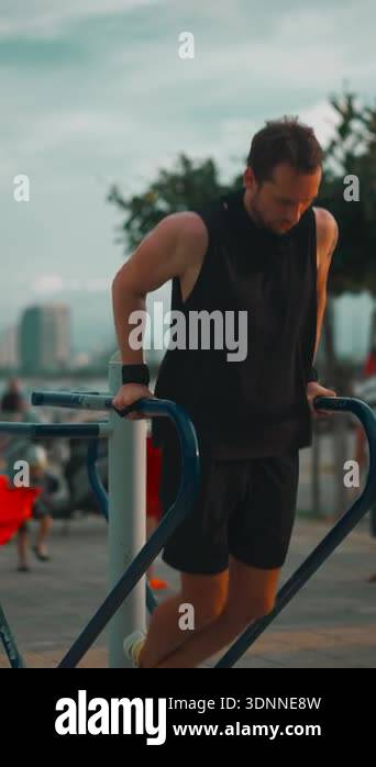 Male bodybuilder performing dips on parallel bars during sunset workout ...