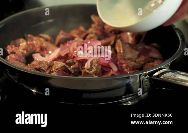 Adding red onion to chicken liver into a frying pan and stirring with a ...