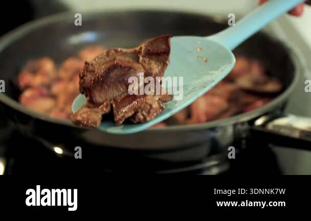 Close up of stirring chicken liver in a pan with a blue silicon spatula ...
