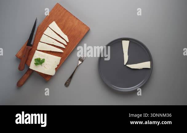 Fresh cheese is cut into slices and arranged on a gray plate in a stop ...