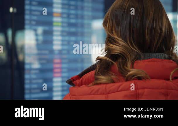 Woman in an orange jacket looks at the flight information board at an ...