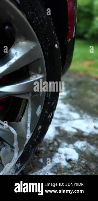 Cleaning car wheel with soap and water in a backyard during a sunny ...