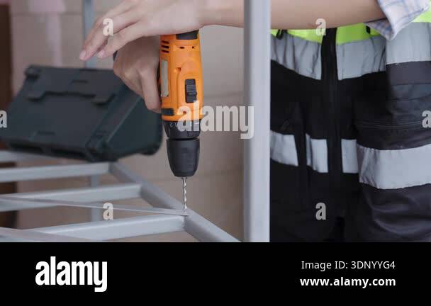 Female workers wearing reflective vests use cordless steel drills to ...