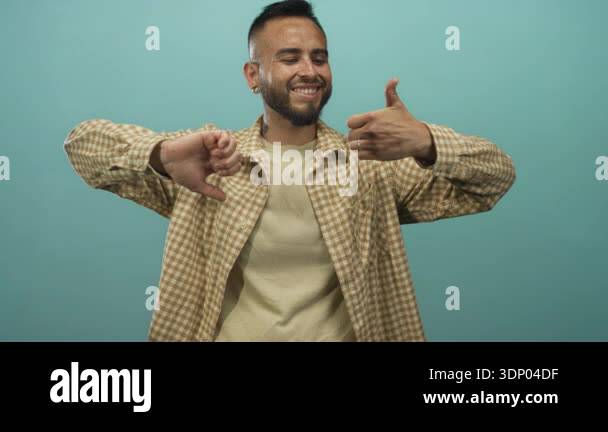 Man showing thumbs up and thumbs down in a studio with a teal backdrop ...