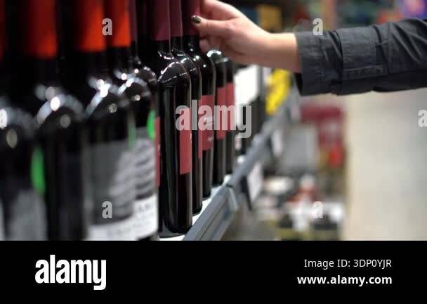 Close up of woman choosing red wine bottle from shelf in supermarket ...