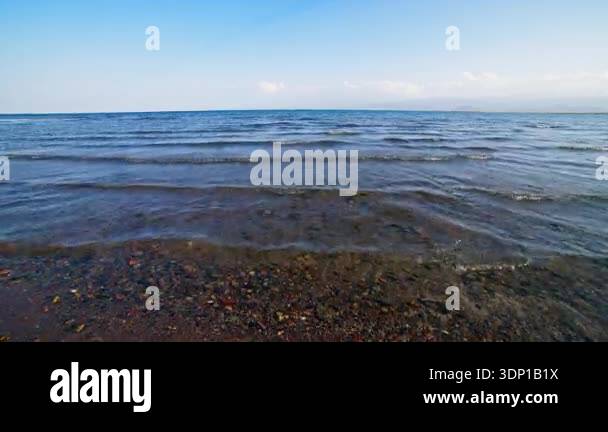Calm beach shoreline with pebbles and gentle surf waves at Issyk-Kul ...