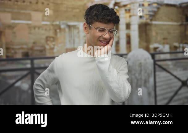 Young hispanic man wearing round glasses touches cheek with hand at ...