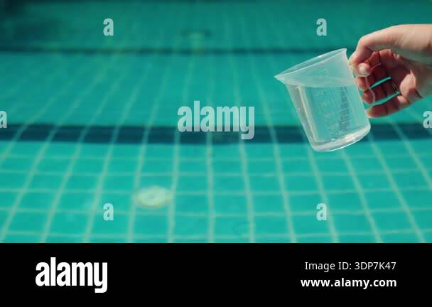 Hand pouring liquid pool chemicals from measuring container into ...