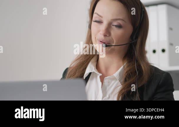 A confident woman in business attire speaks into a headset while ...