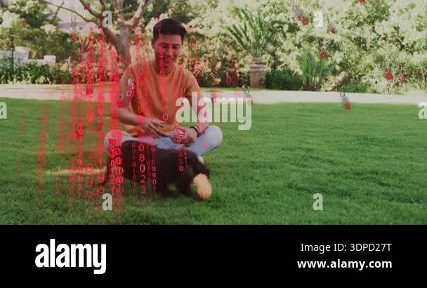 Man cross-legged coaxing black puppy jumping at orange toy red binary ...