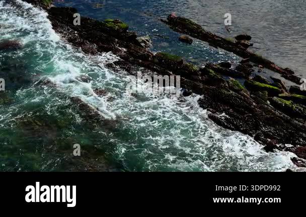 Waves rolling against moss covered coastal stones. Surf washing over ...