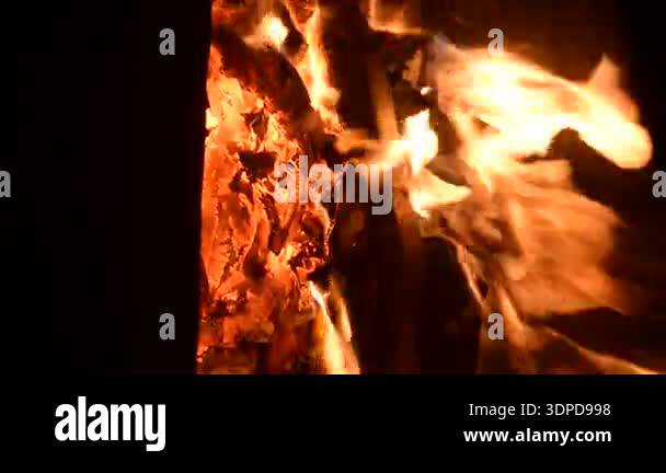 Close-up of burning wood with glowing embers and bright orange flames ...