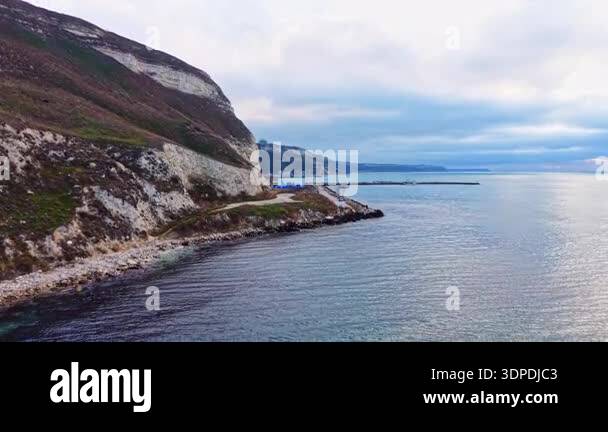 A coastal area with cliffs rising above the water. A small path runs ...