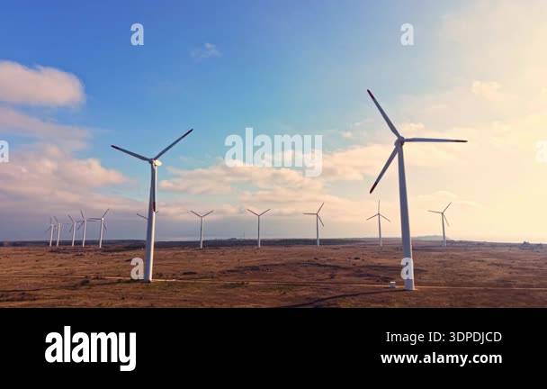 Wind turbines are arranged in a line in a large open field under a blue ...