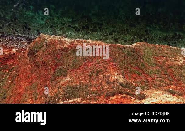 A rocky coastline shows texture and color as clear water meets land ...