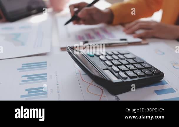 A person calculating financial data on a calculator with graphs and ...