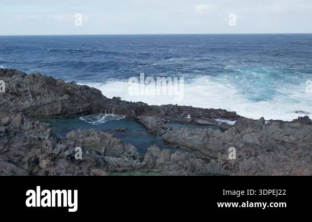 Huge ocean waves crashing on a rugged volcanic rock coast with natural ...