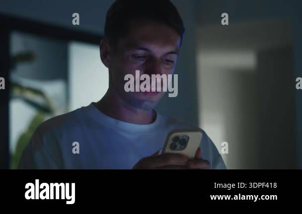 Young man using smartphone at night, glowing screen lighting his face ...