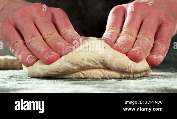 Slow motion closeup of a bakers hands kneading and stretching freshly ...