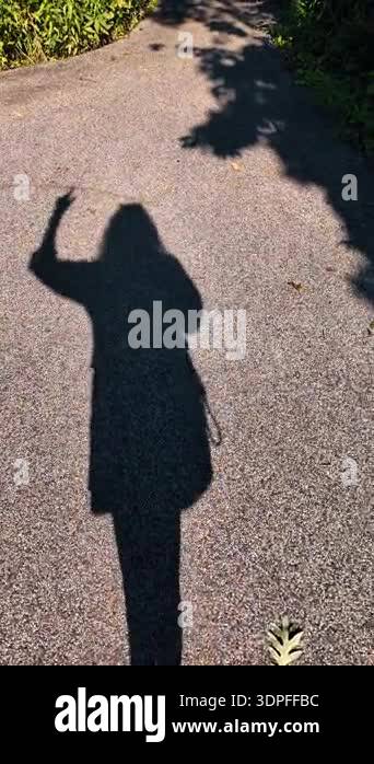 Shadow of a female figure taking video. Shadow on the asphalt alley ...